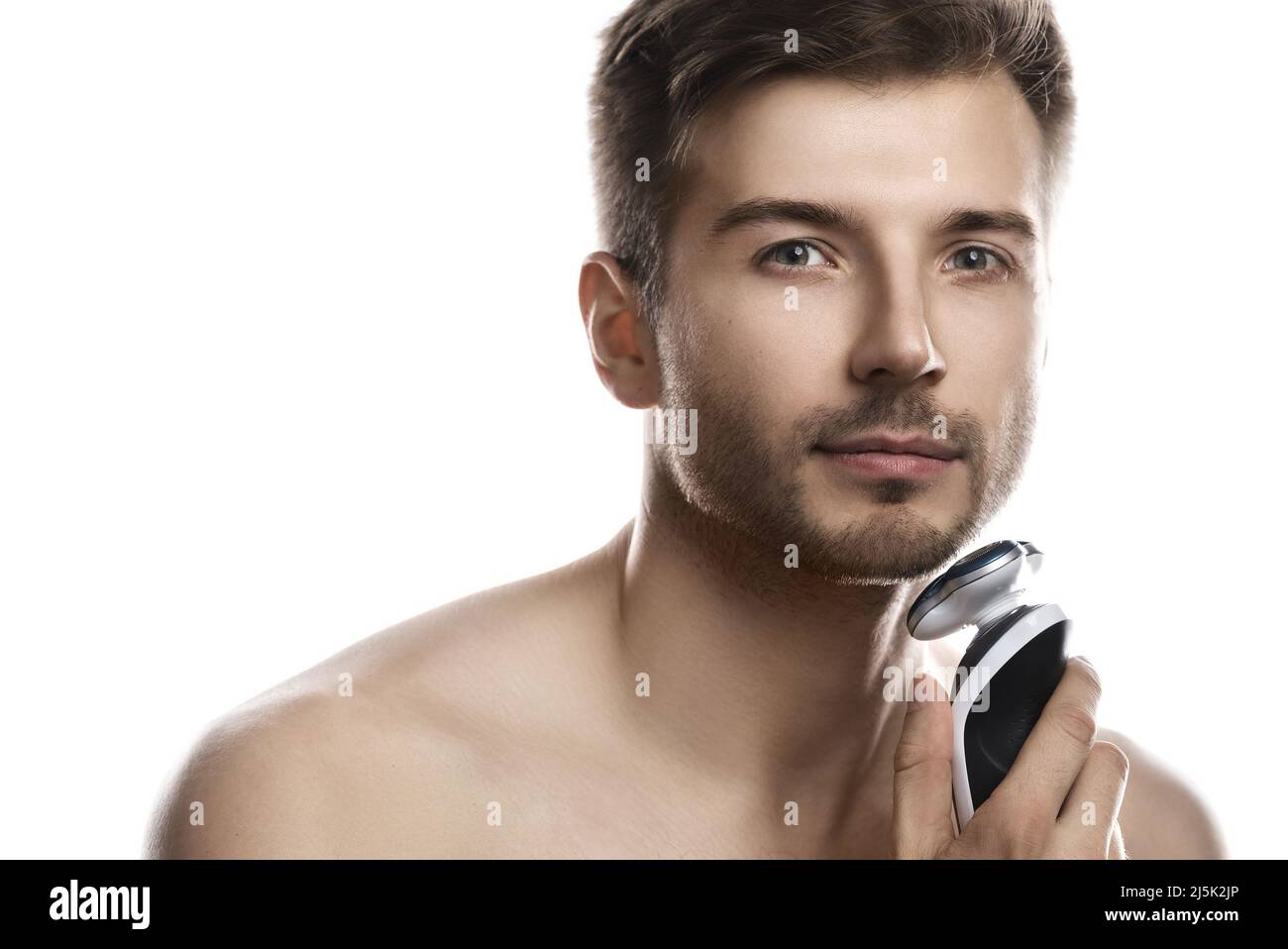 Young and handsome man is using modern electric shaver on white ...