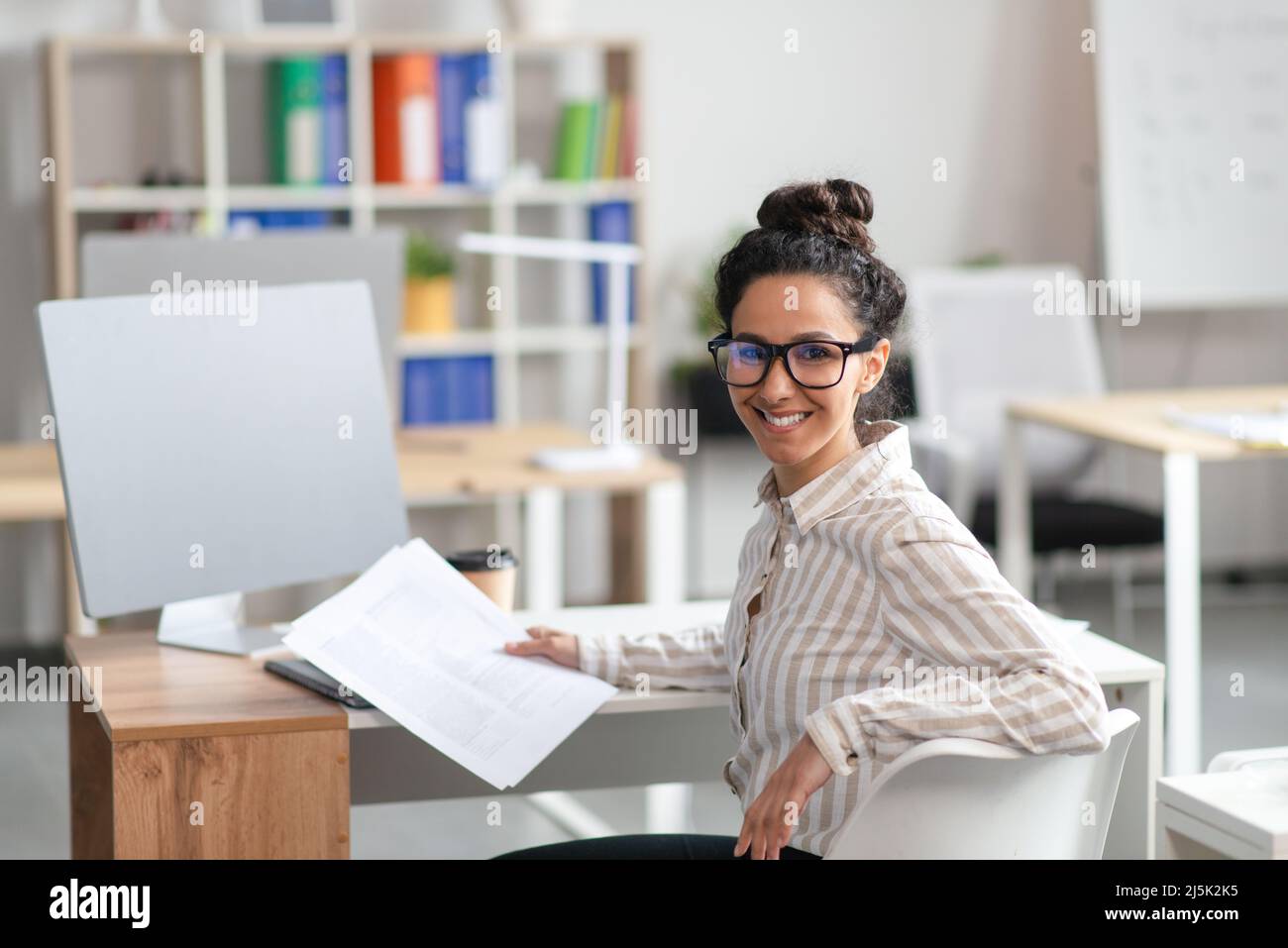 Cheerful latin female general manager checking reports in modern office ...