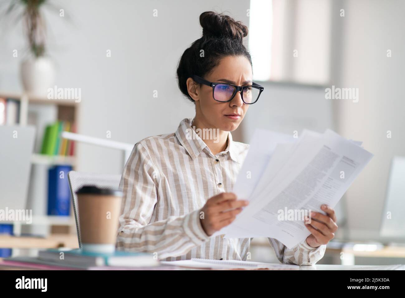 Paperwork concept. Focused female manager holding and reading paper or ...