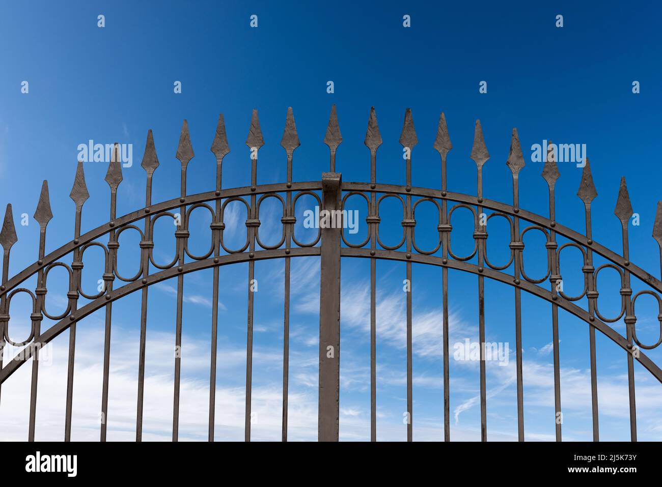 Close-up of a wrought iron gate with sharp points on blue sky with ...