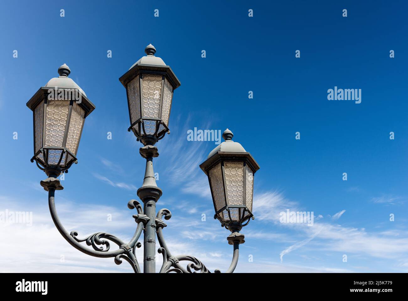 Old street lamp posts against a clear blue sky with clouds and copy ...