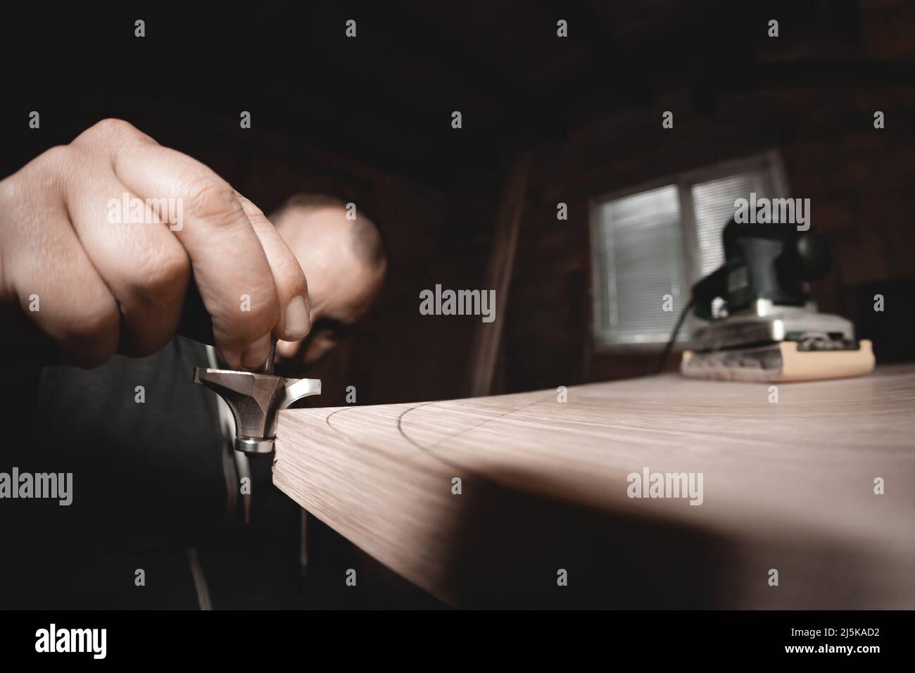 Carpenter with hand electric router machine at work. Trying on a cutter ...