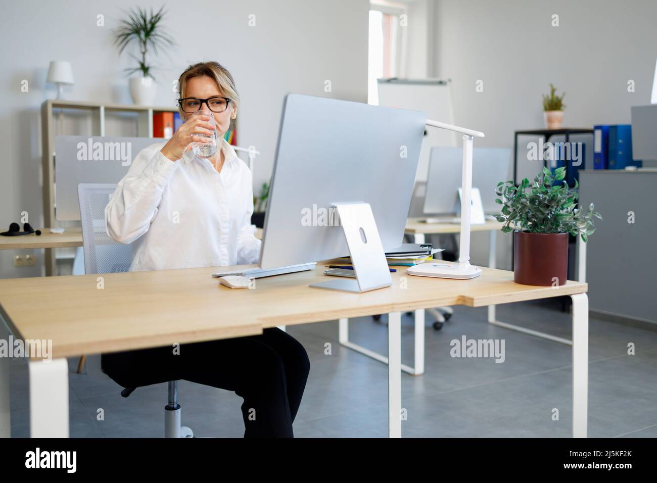 Pretty adult business woman in the office drinking water while working ...