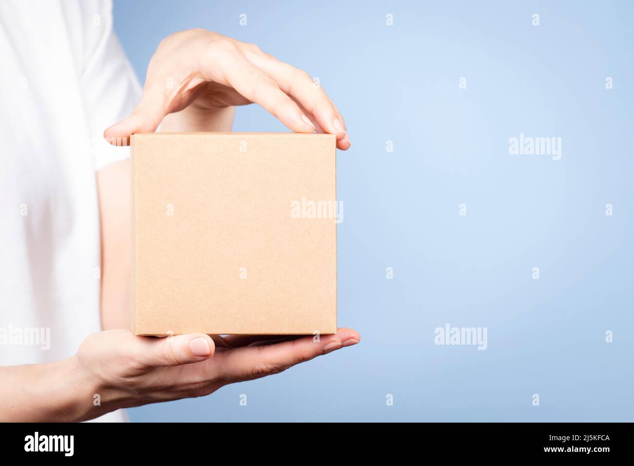 Female hands holding brown rectangular cardboard box on light blue ...