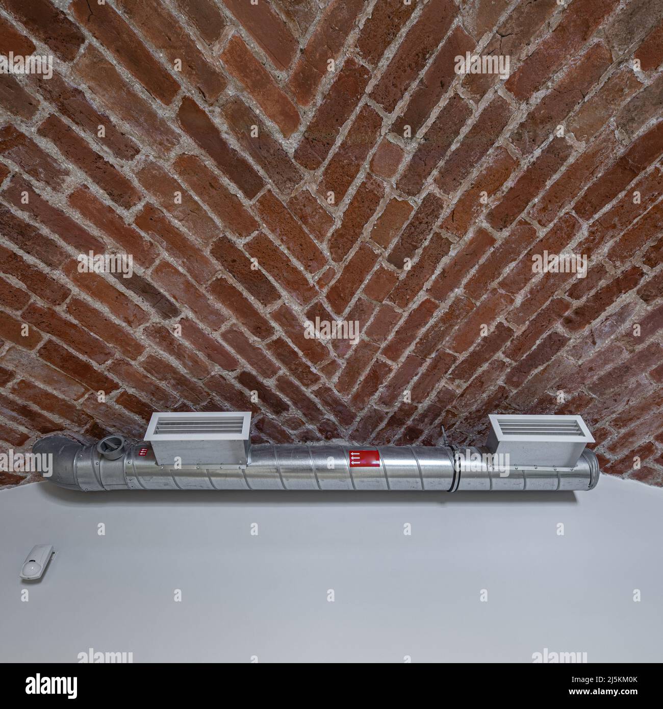 Brick ceiling and metal ventilation pipe. White wall. Old style ...