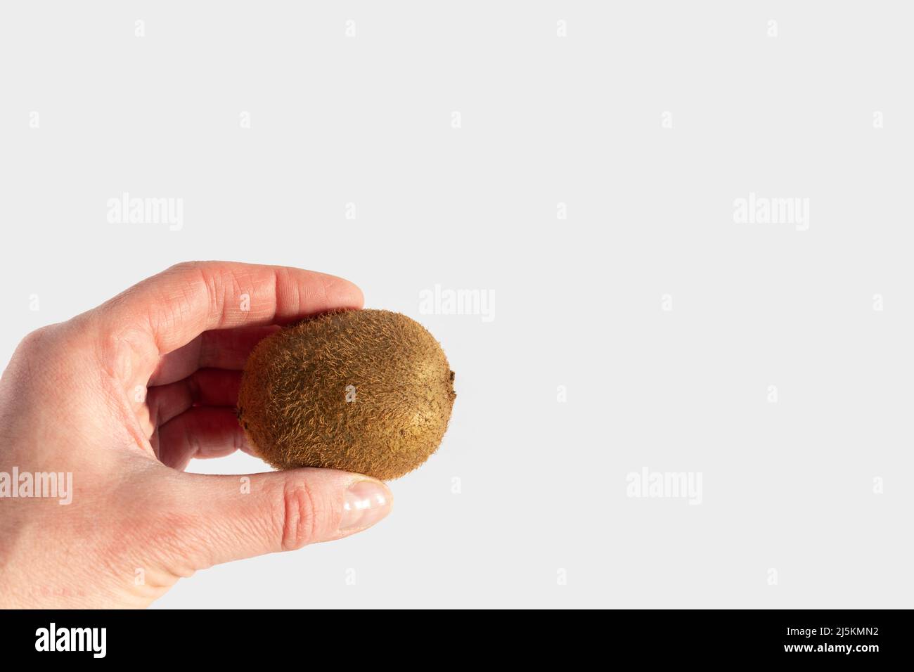 Hand holding ripe unpeeled kiwi fruit on white background, copy space ...