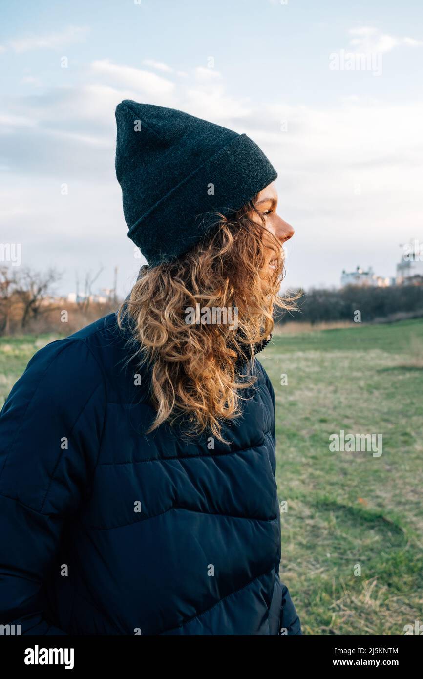Side view portrait young woman in hat and down jacket walks in nature ...