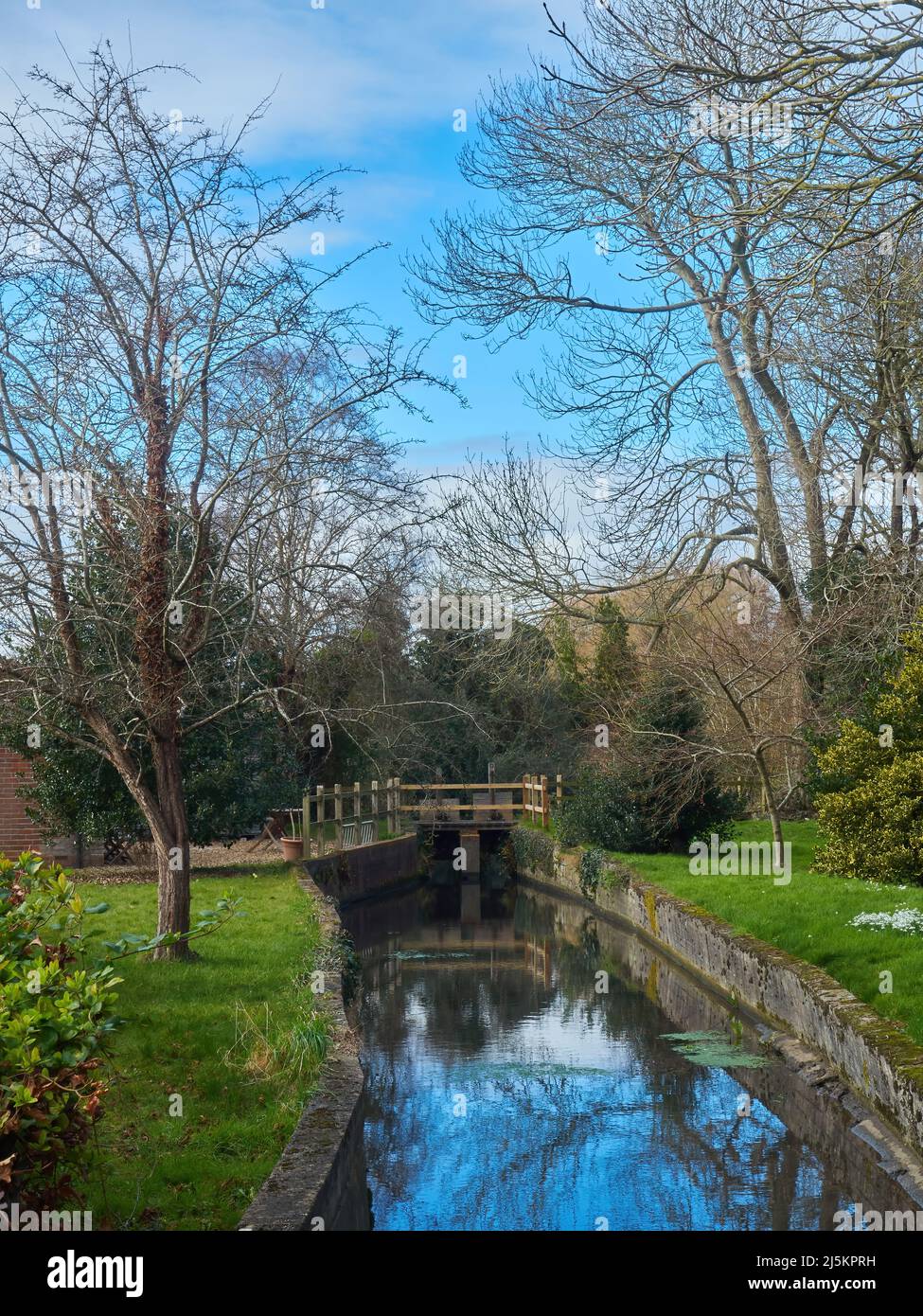 A small wooden bridge over the still, glassy waters of a tree-lined ...