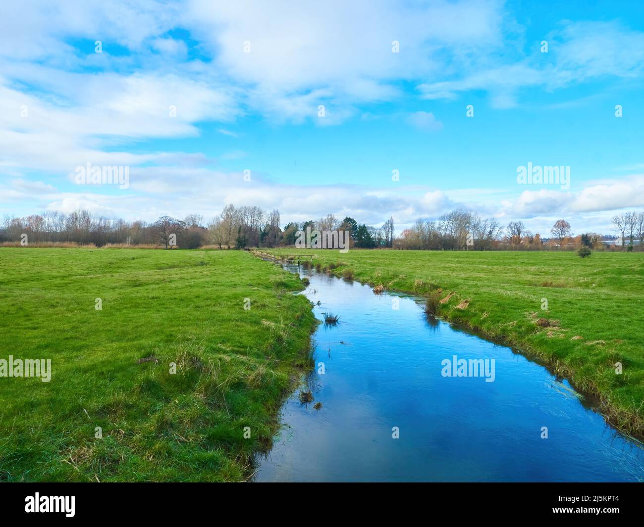 A glassy stream reflects blue sky as it meanders through a wide-open ...