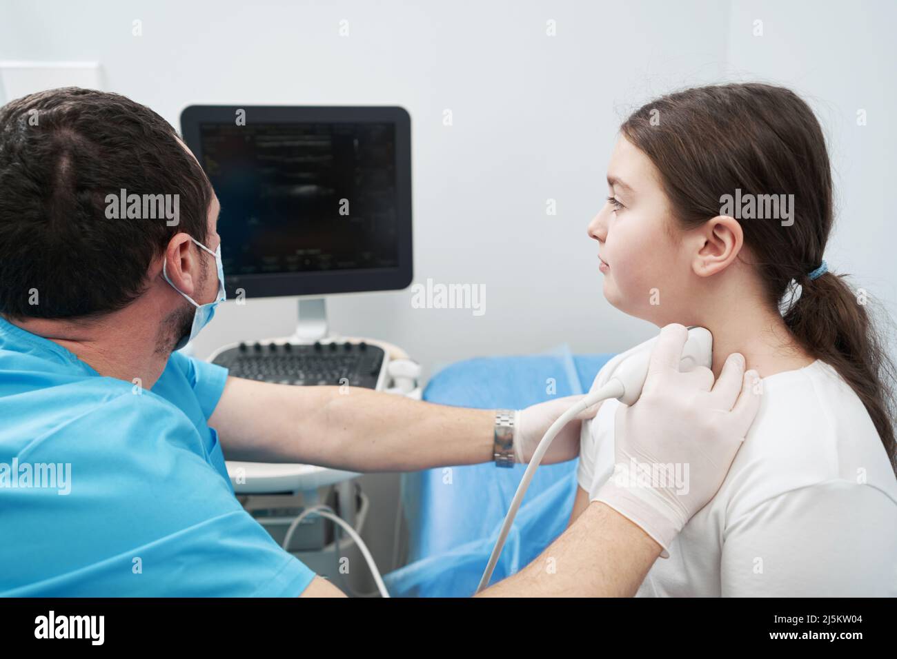 Medical worker examining girl thyroid gland with an ultrasound machine ...