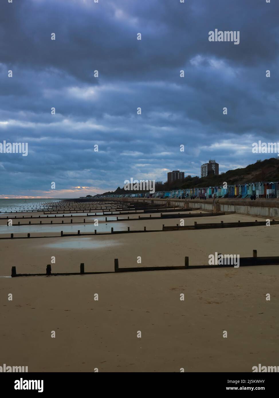 Colourful beach huts, an esplanade and a groyne-divided beach in ...