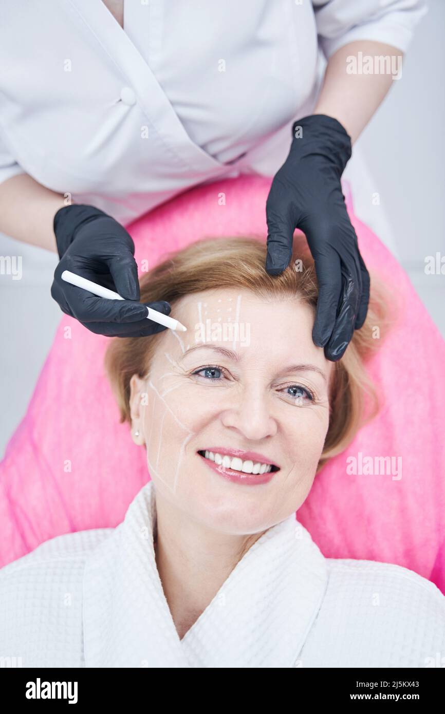 Beautician drawing marks on woman forehead in beauty salon Stock Photo ...