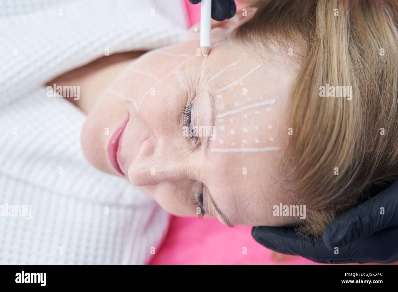 Cosmetologist drawing line on woman face with white pencil Stock Photo ...