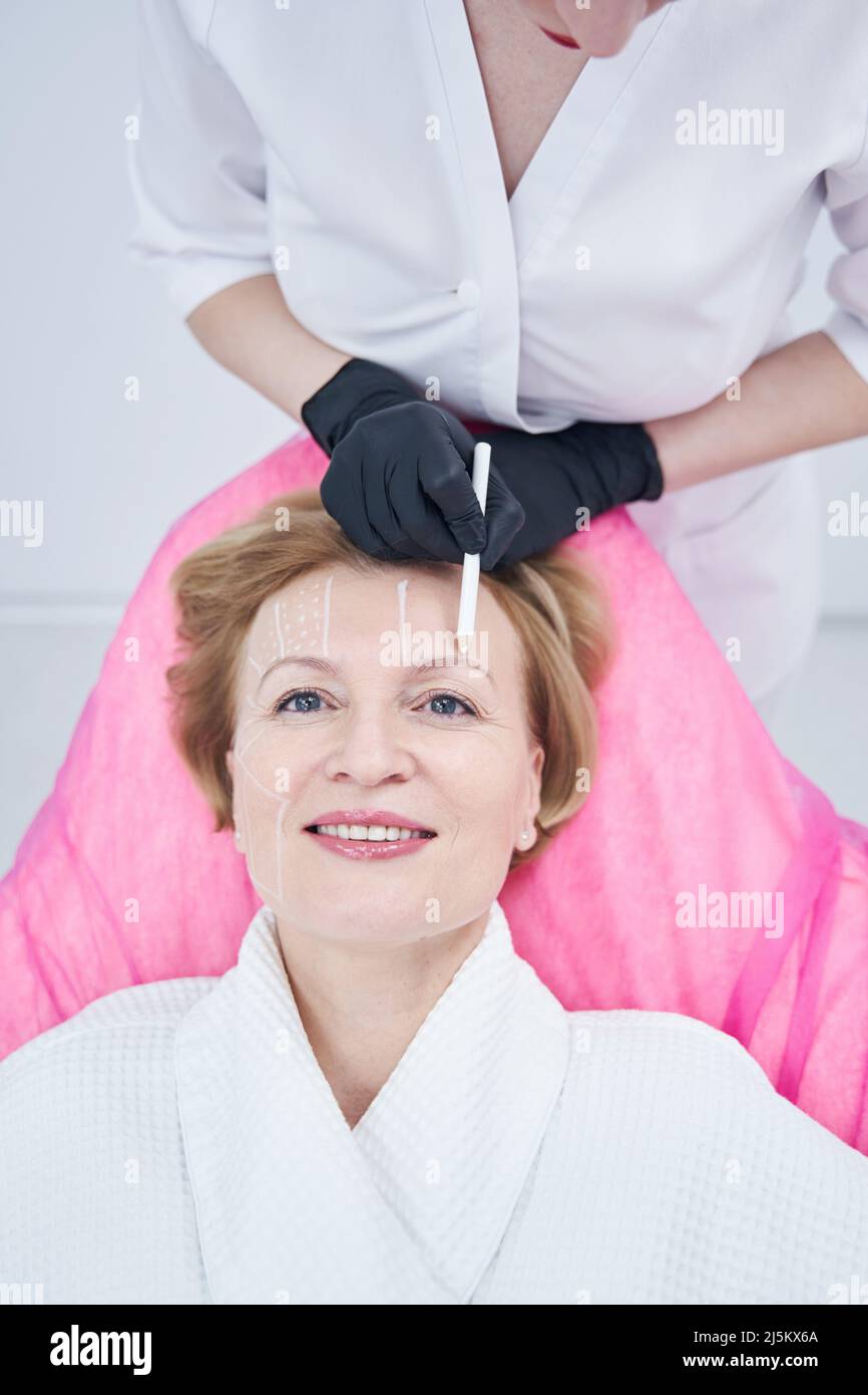 Cosmetologist drawing marks on woman face in cosmetology clinic Stock ...