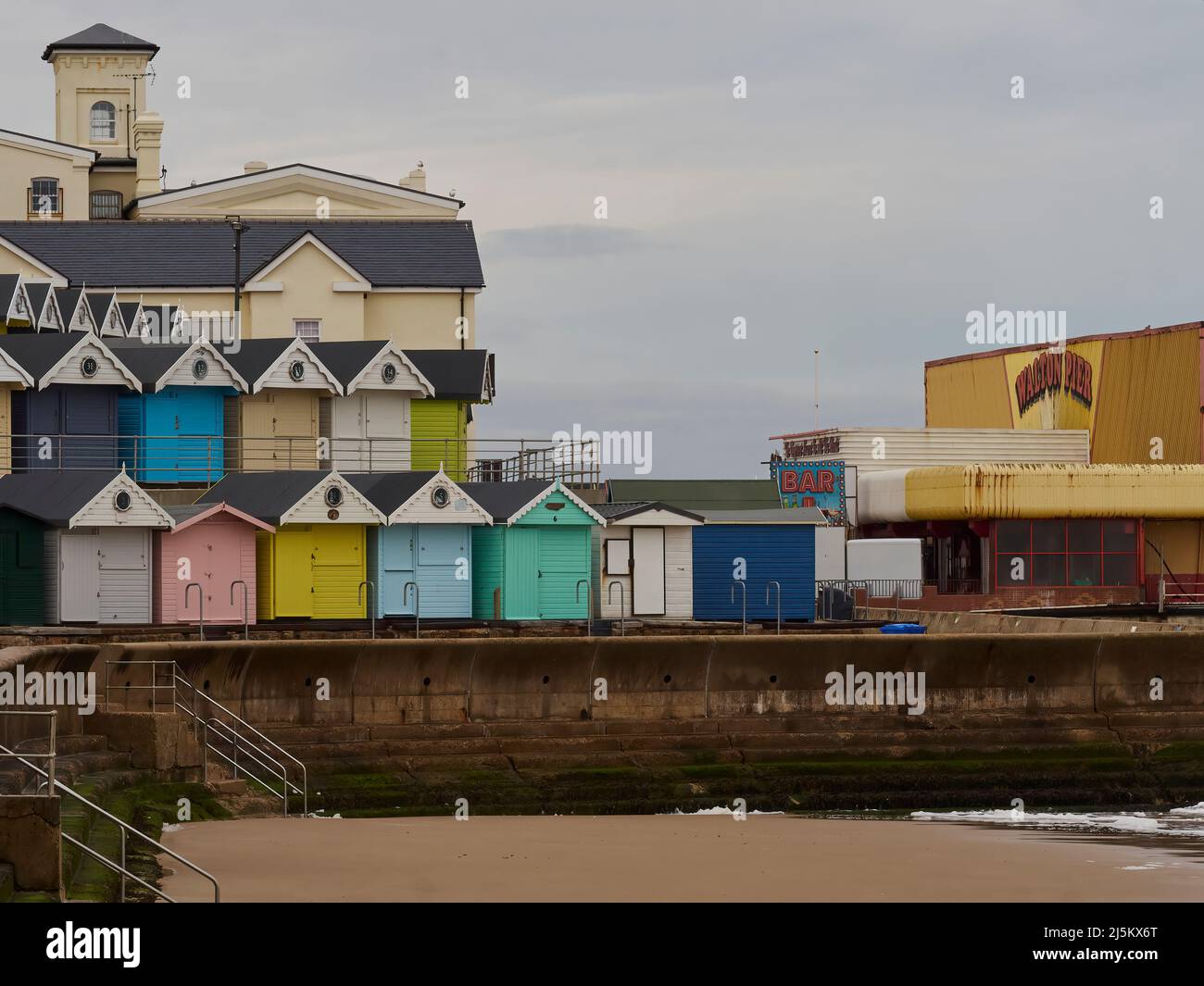 Colourful beach huts on a hill curving to a derelict looking fun fair ...