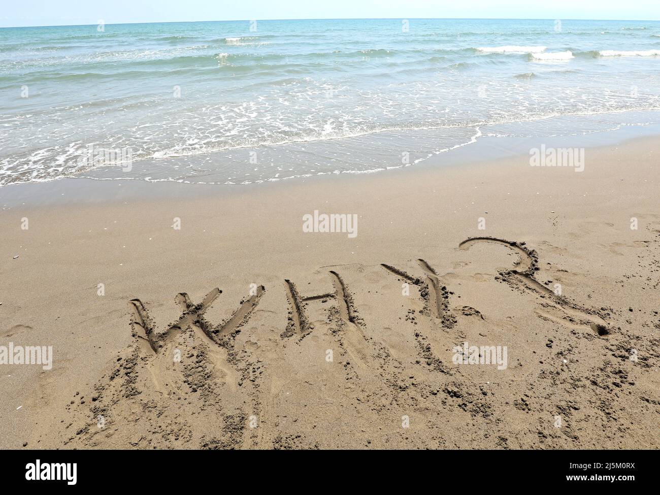 big text WHY with question mark that was written in the sand by the sea ...