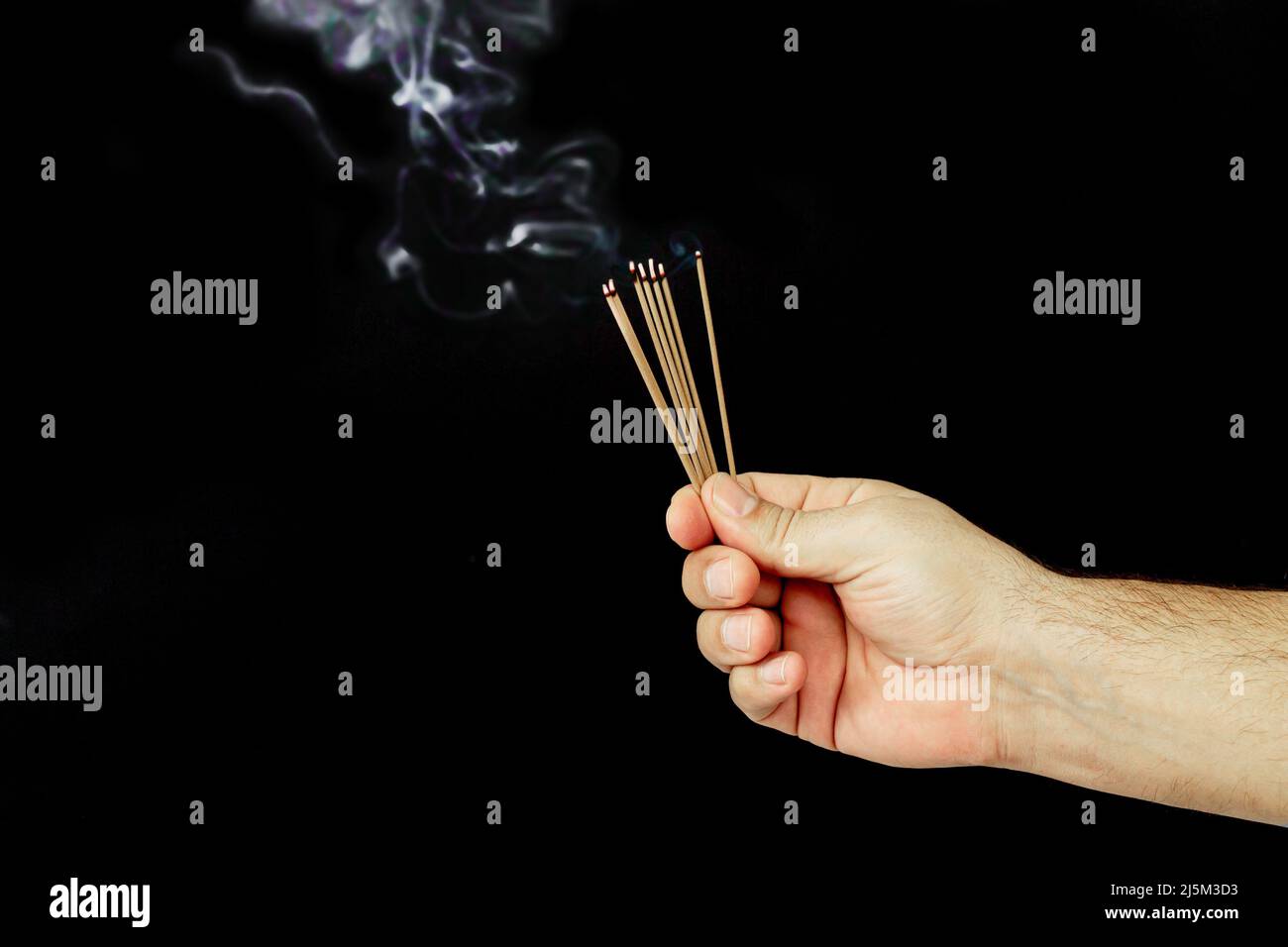 Male hand holding set of smoldering incense sticks with aroma smoke on ...