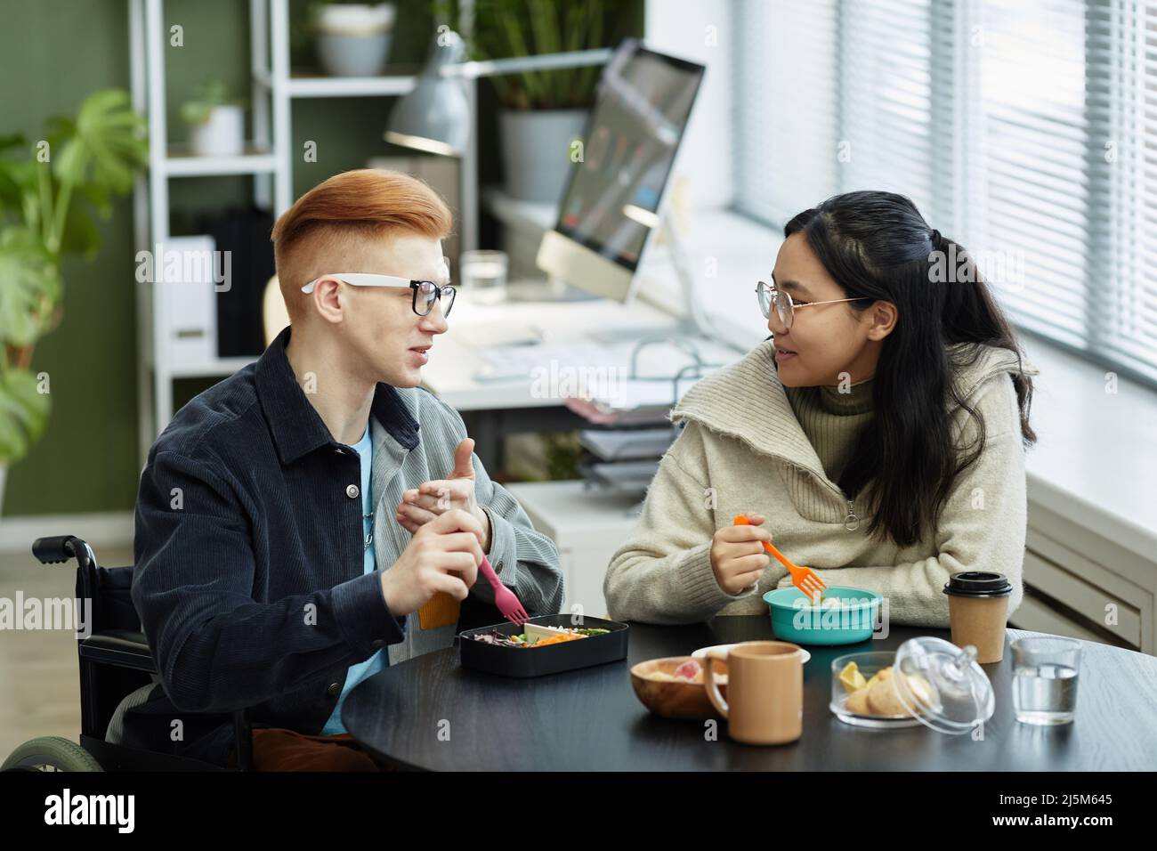 Side view portrait of two smiling young people eating lunch at work and ...