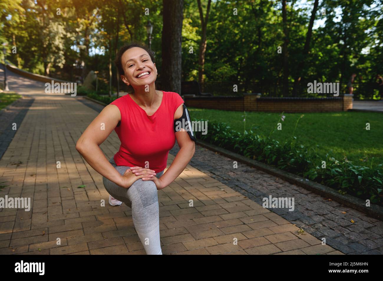 Happy cheerful African woman doing lunges while exercising outdoor ...