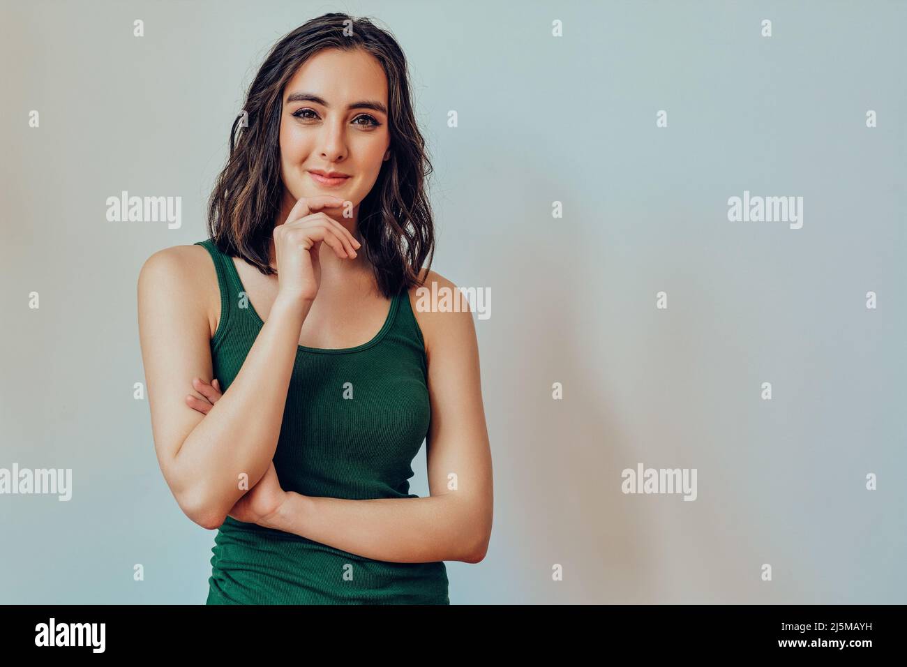 Woman with hand on chin arms crossed on white background looking at ...