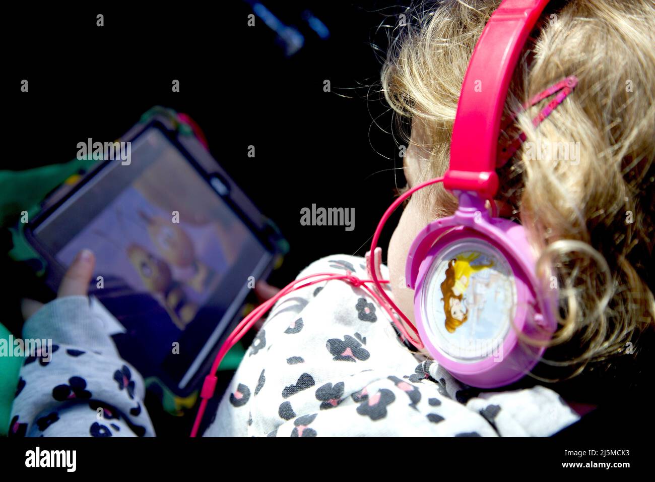 3 year old girl watching cartoons on her iPad wearing headphones while ...