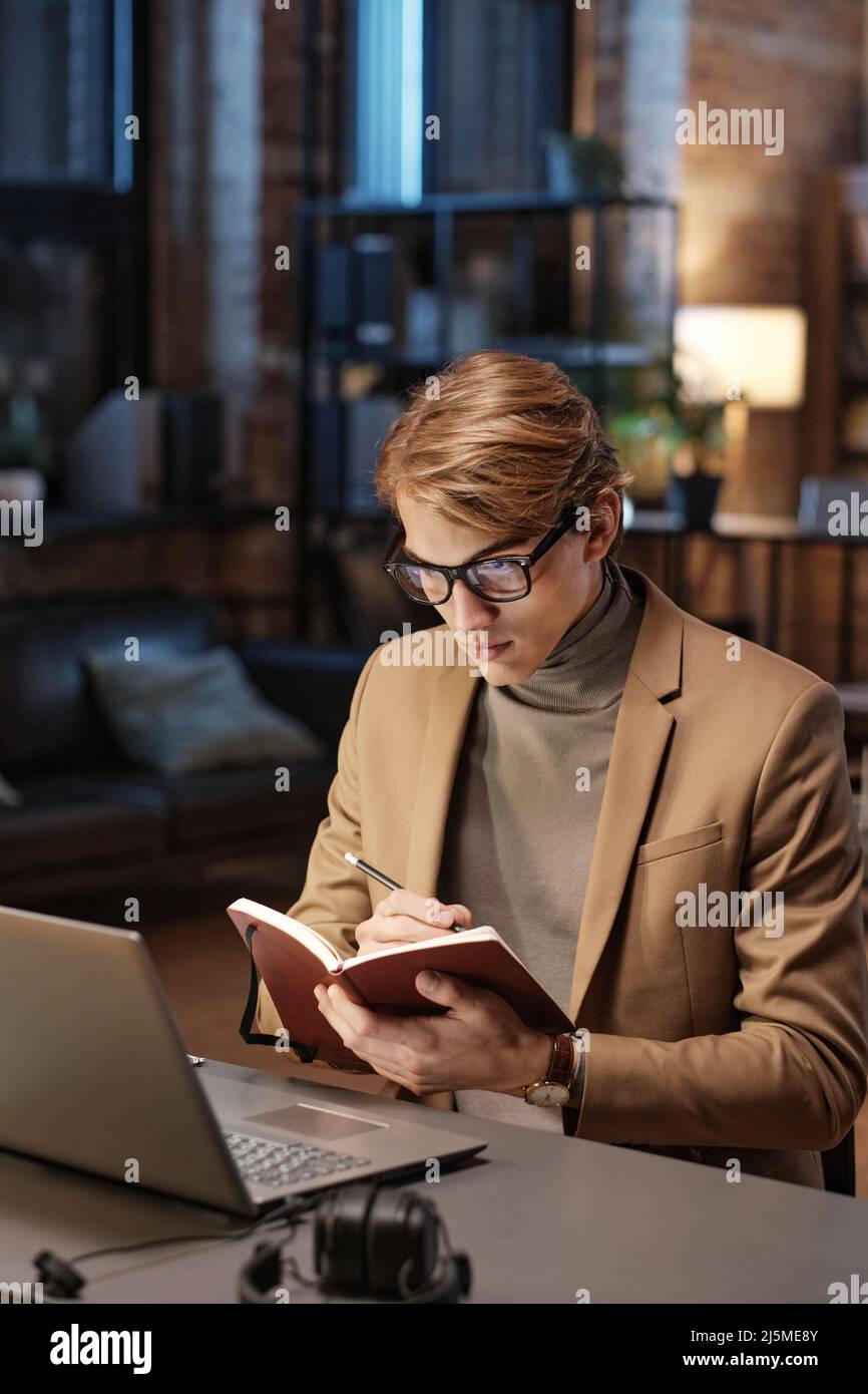 Concentrated young manager making notes in diary and viewing report ...