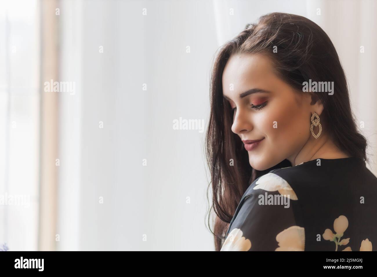 Side view portrait of attractive smiling girl with lowered eyes indoors ...