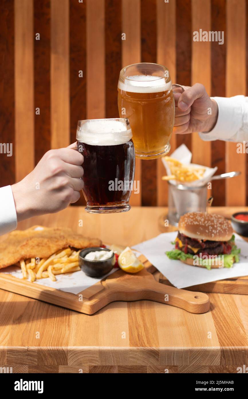 Closeup of two hands clinking beer stein glasses. Toasting with a pint ...