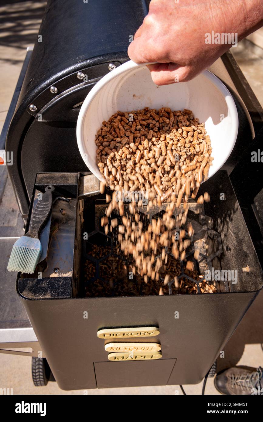 Pitmaster pours fresh hardwood pellets into the hopper of a smoker ...