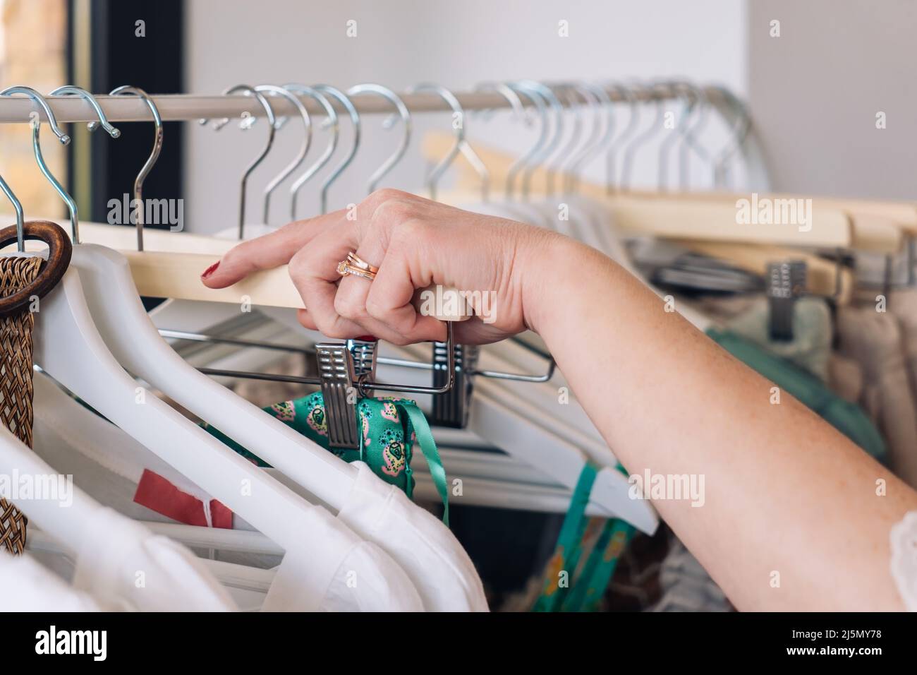 hand of a woman picking up a clothes from a hanger in a fashion shop ...