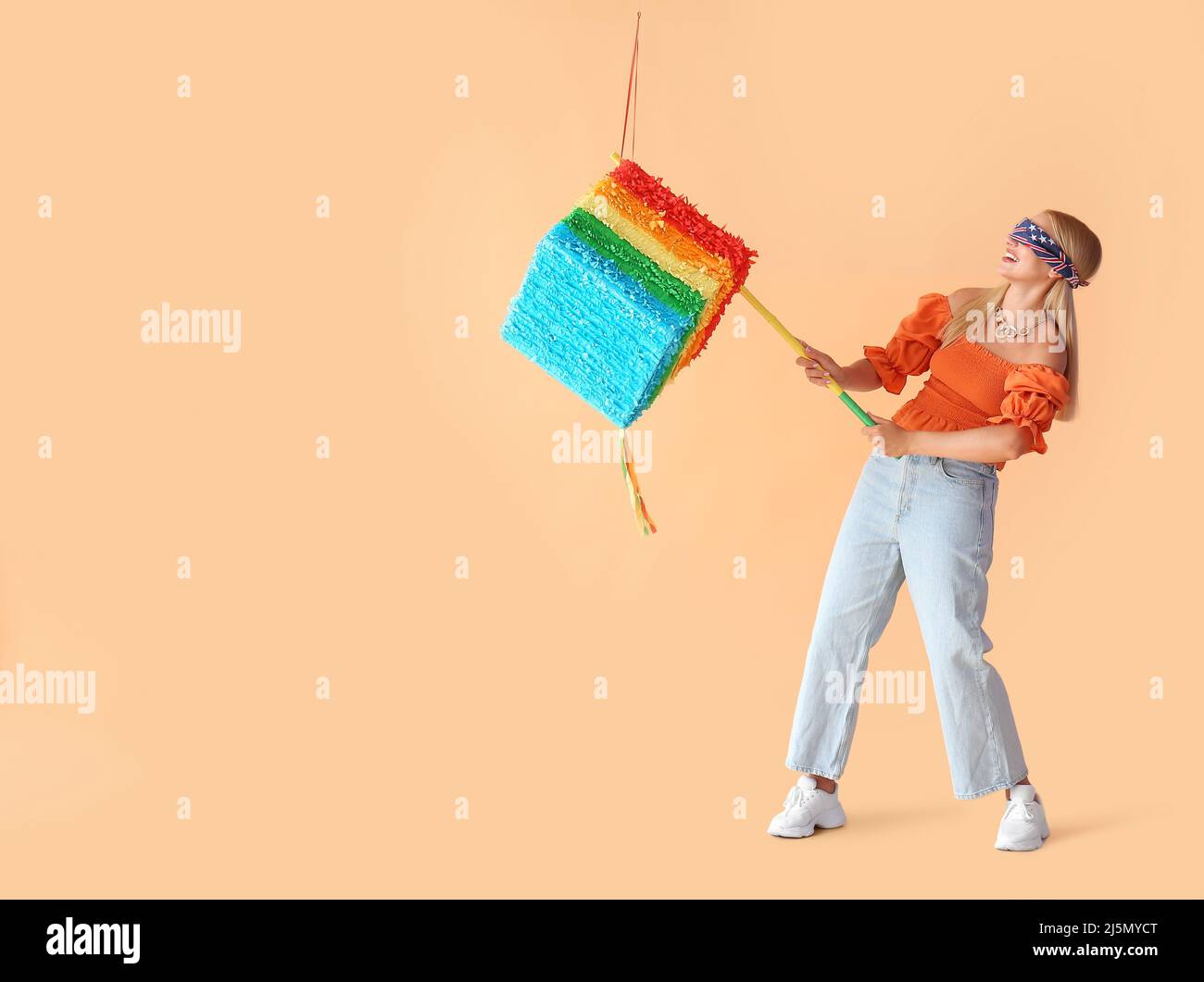 Young woman with blindfold breaking Mexican pinata on beige background ...
