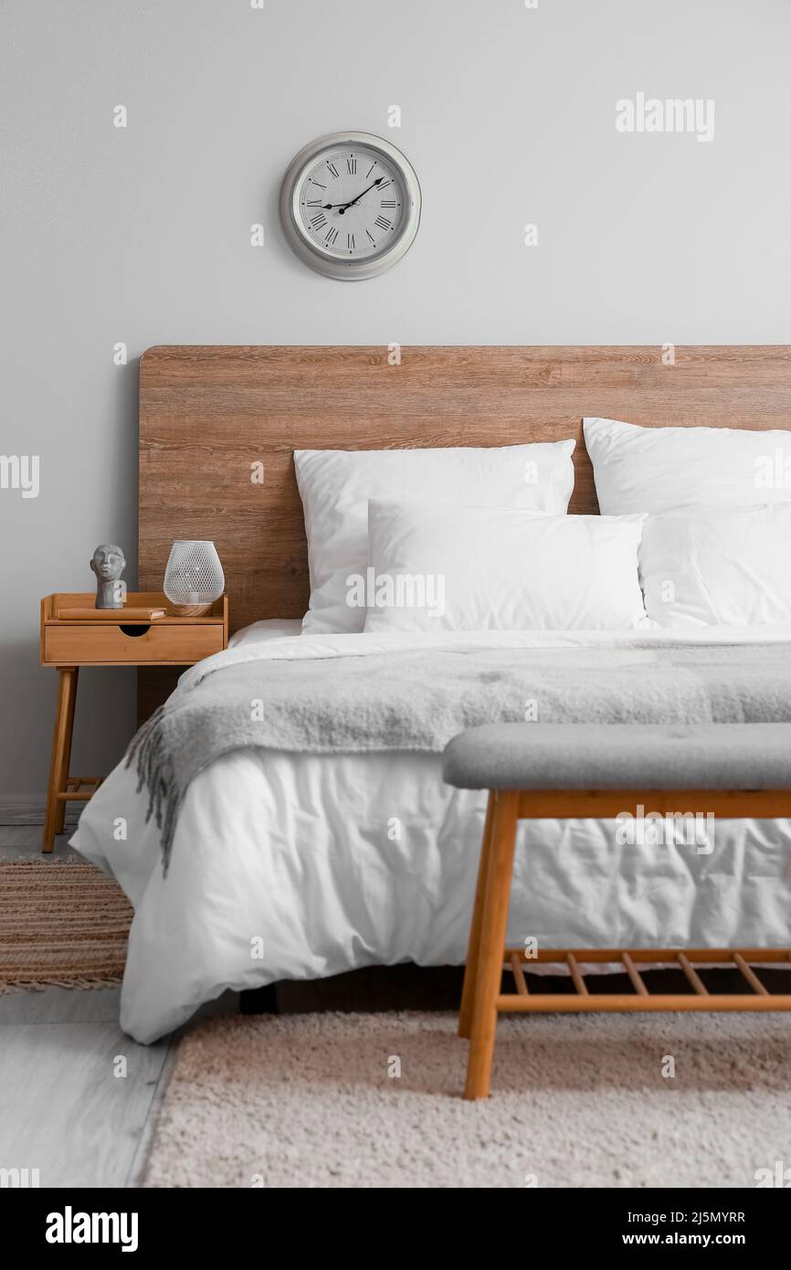 Comfortable bed, bedside table with stylish decor and clock on light ...