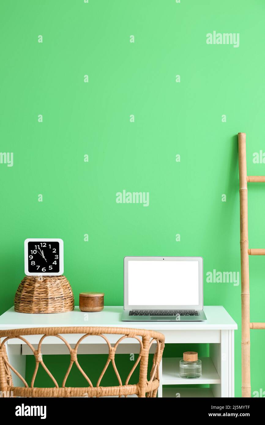 Modern workplace with laptop and clock near green wall Stock Photo - Alamy