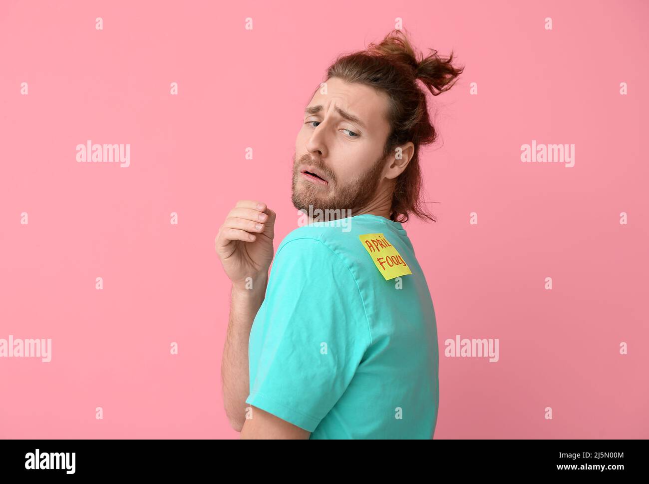 Sad man with sticky note on his back against pink background. April ...