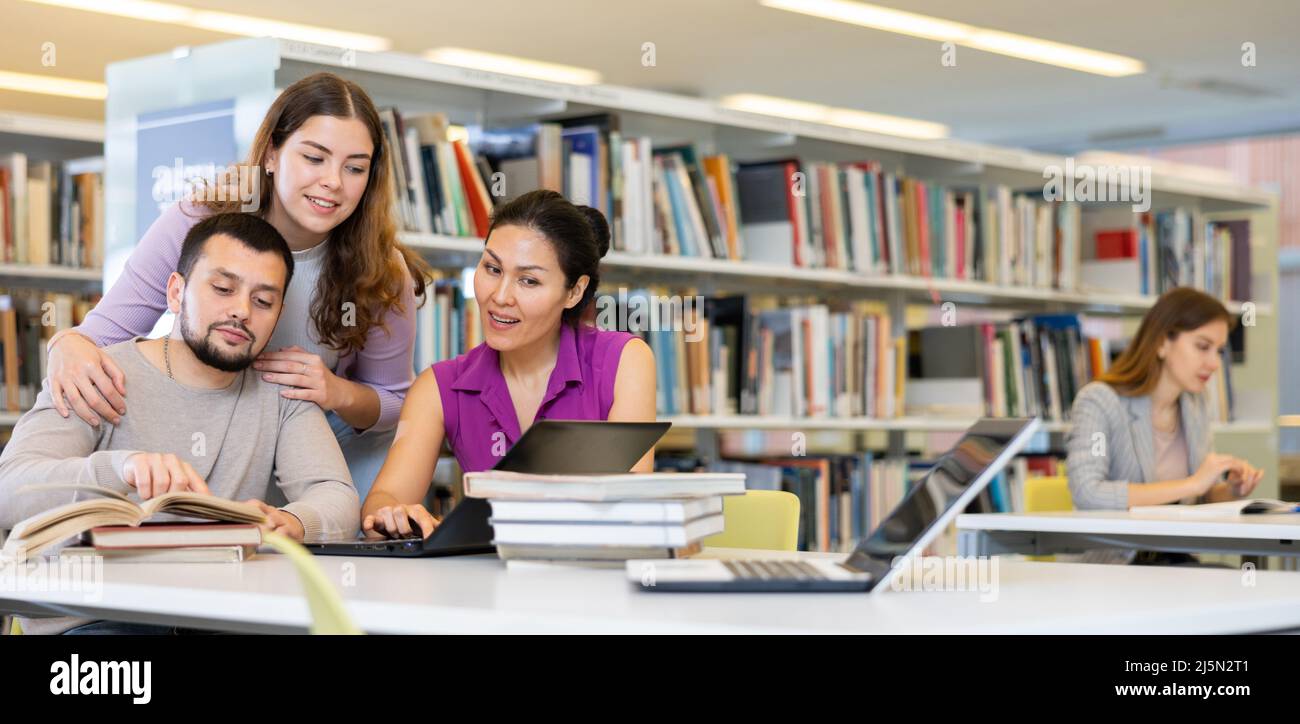 Three adult students work on laptop and read books in a public library ...