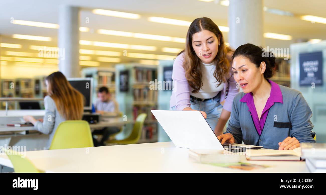 Two female scientists using books and laptop for research in library ...