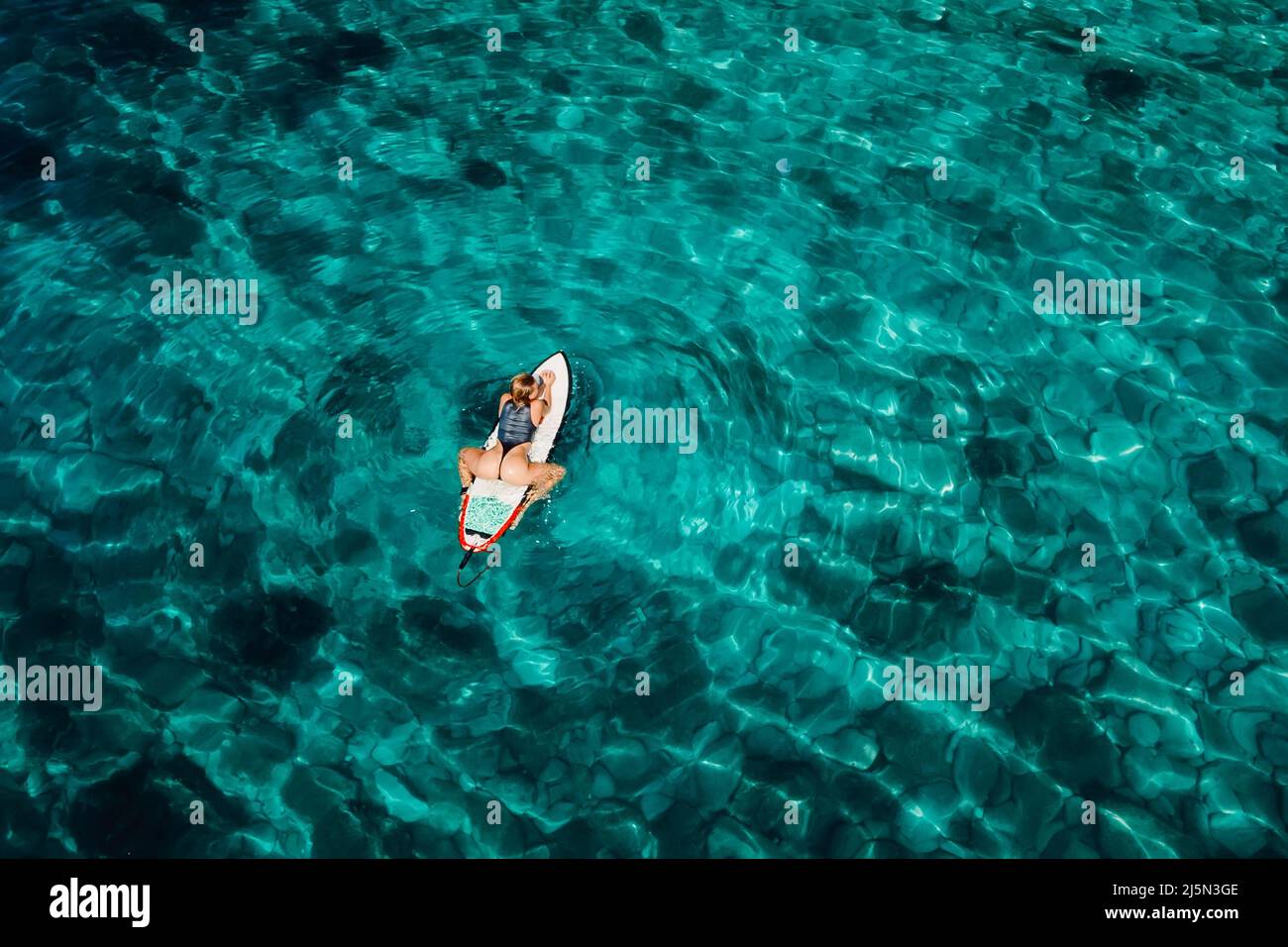 Surf girl on surfboard wait surfing wave in transparent ocean. Aerial ...