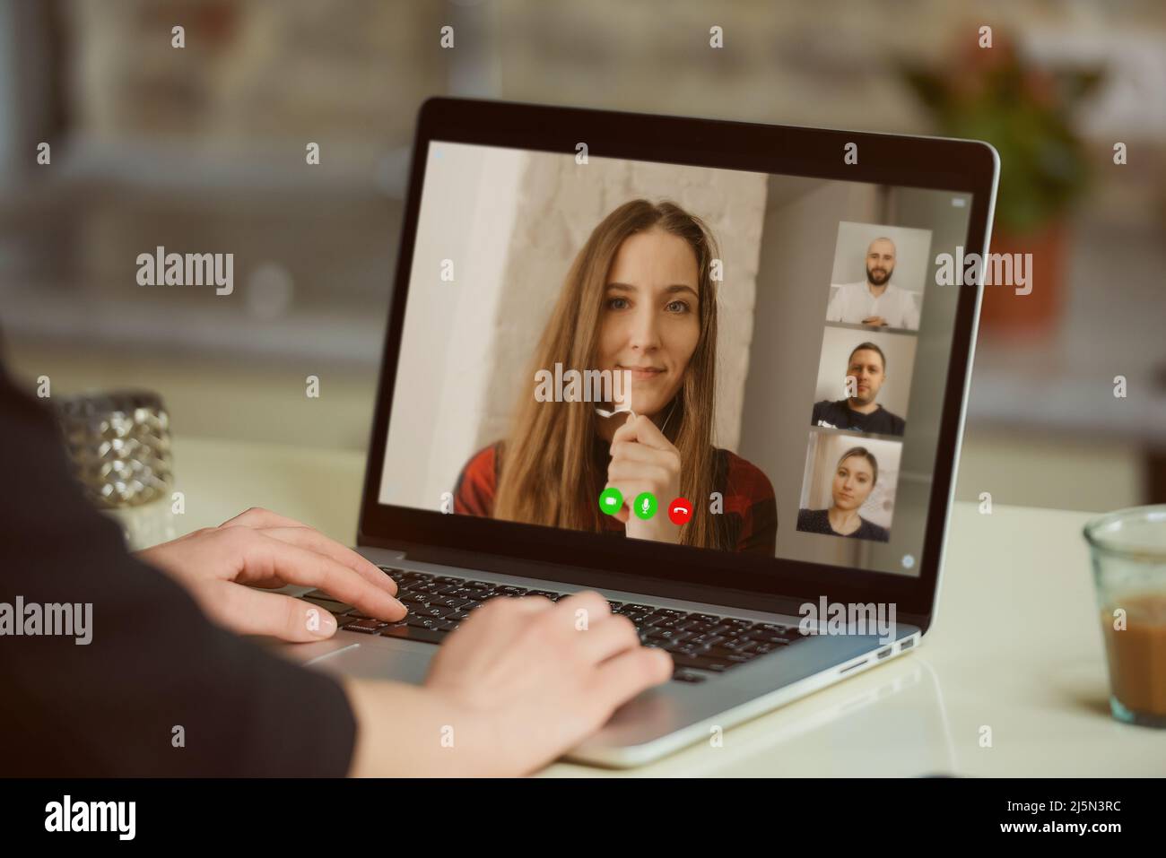 Laptop screen view over a woman's shoulder. A girl works remotely on a ...