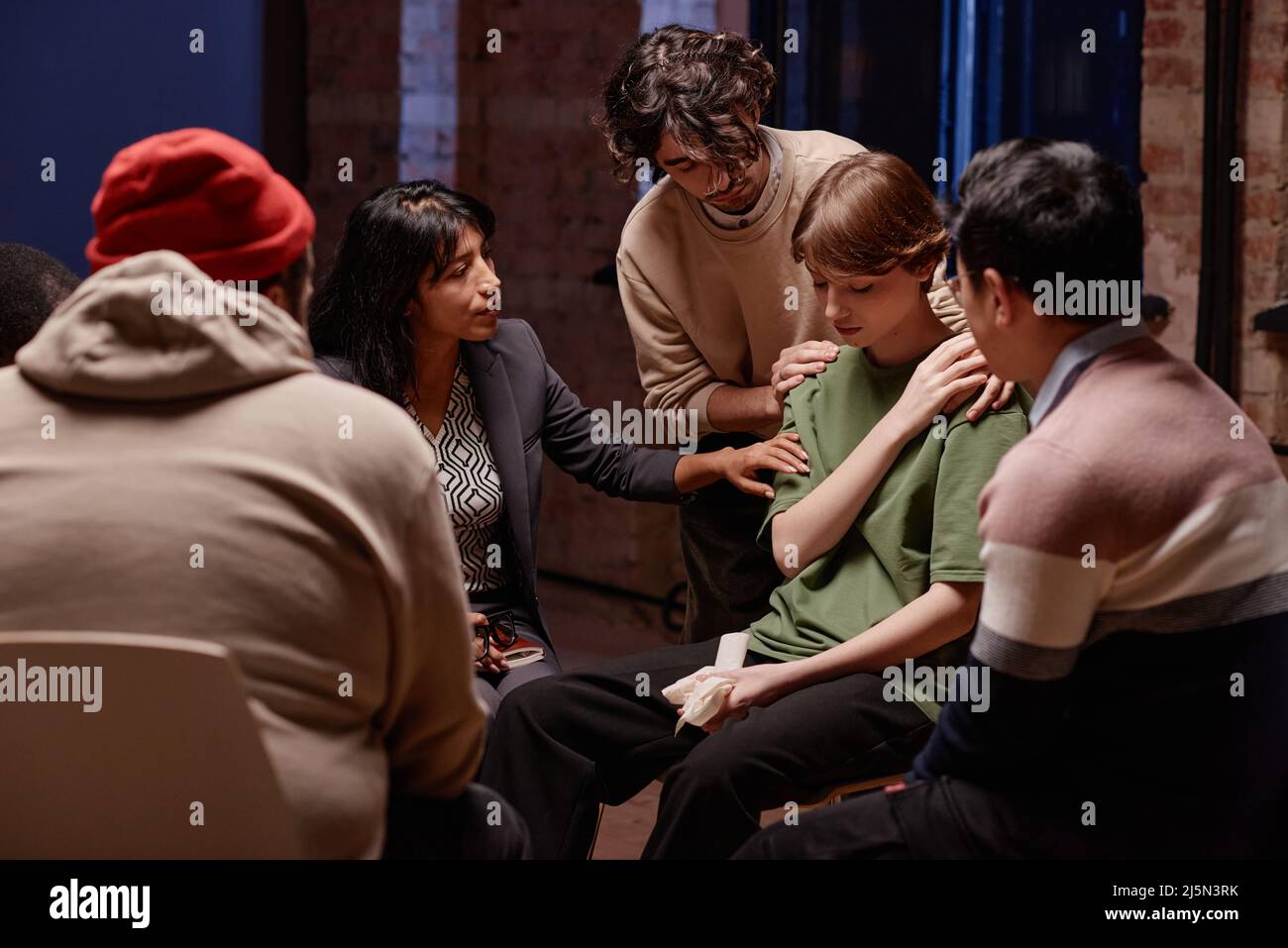 Horizontal shot of psychologist and clients comforting young woman ...