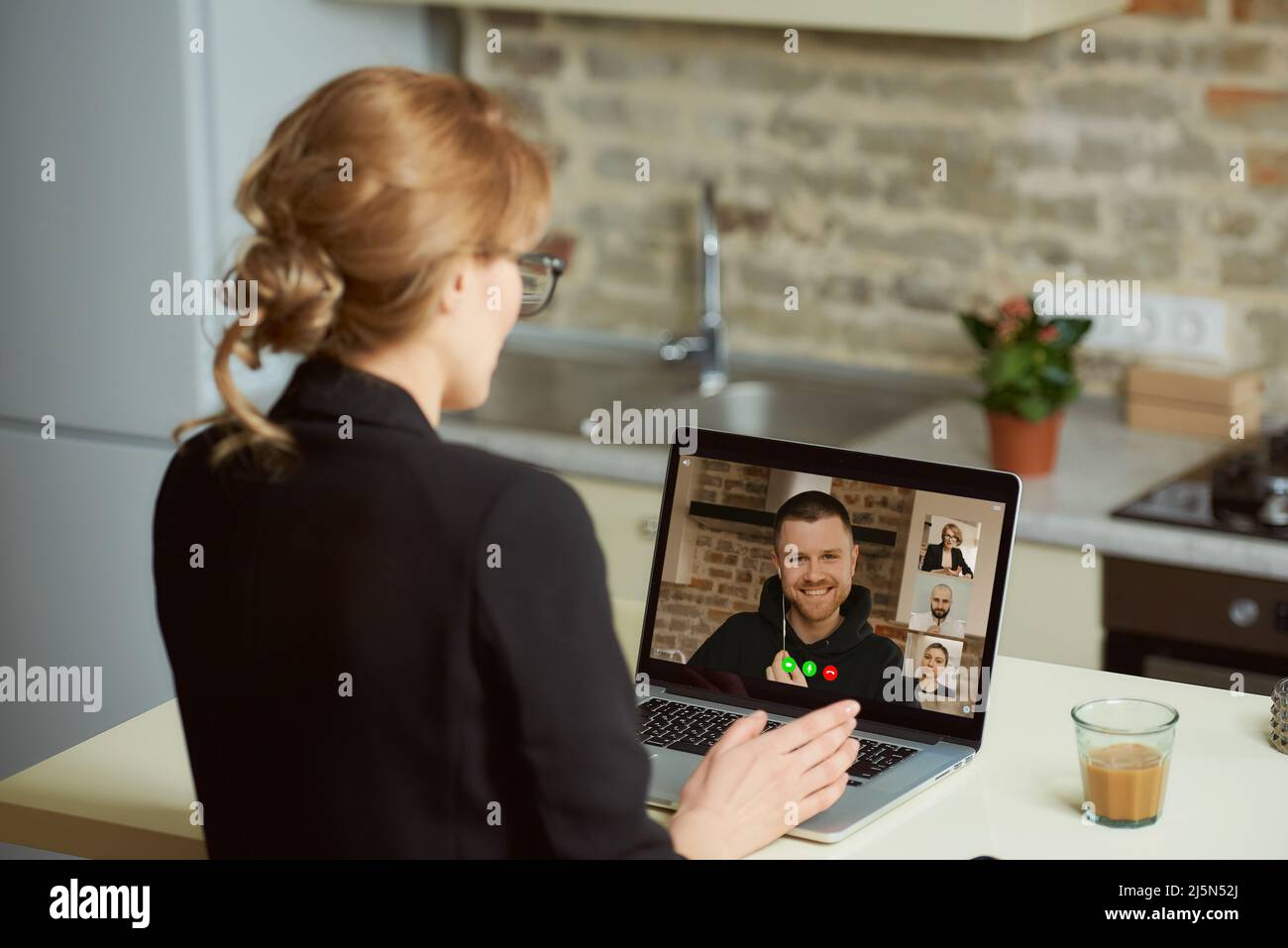 Laptop screen view over a woman's shoulder. A girl works remotely on a ...