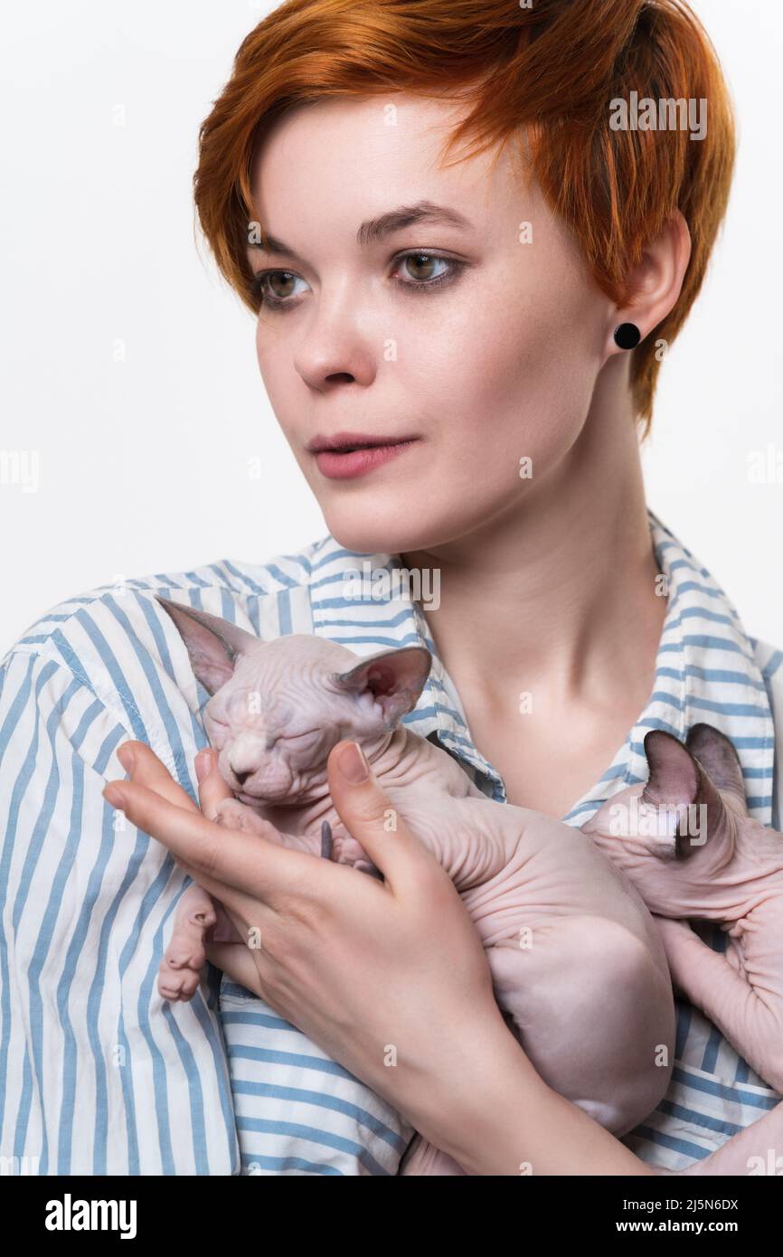 Beautiful redhead young woman hugging Sphynx Cat and looking away ...