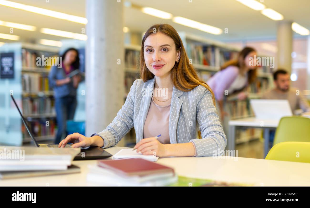 Young woman sitting in library with laptop and books Stock Photo - Alamy