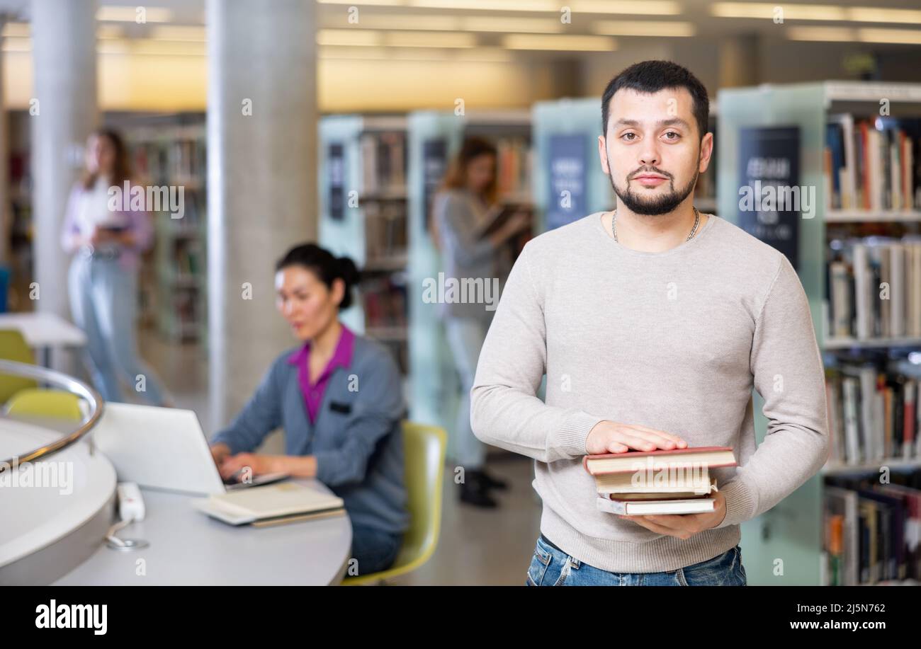 Portrait of man holding books at library Stock Photo - Alamy