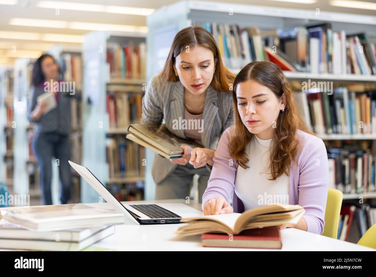 Two positive women working with books and laptop in library Stock Photo ...