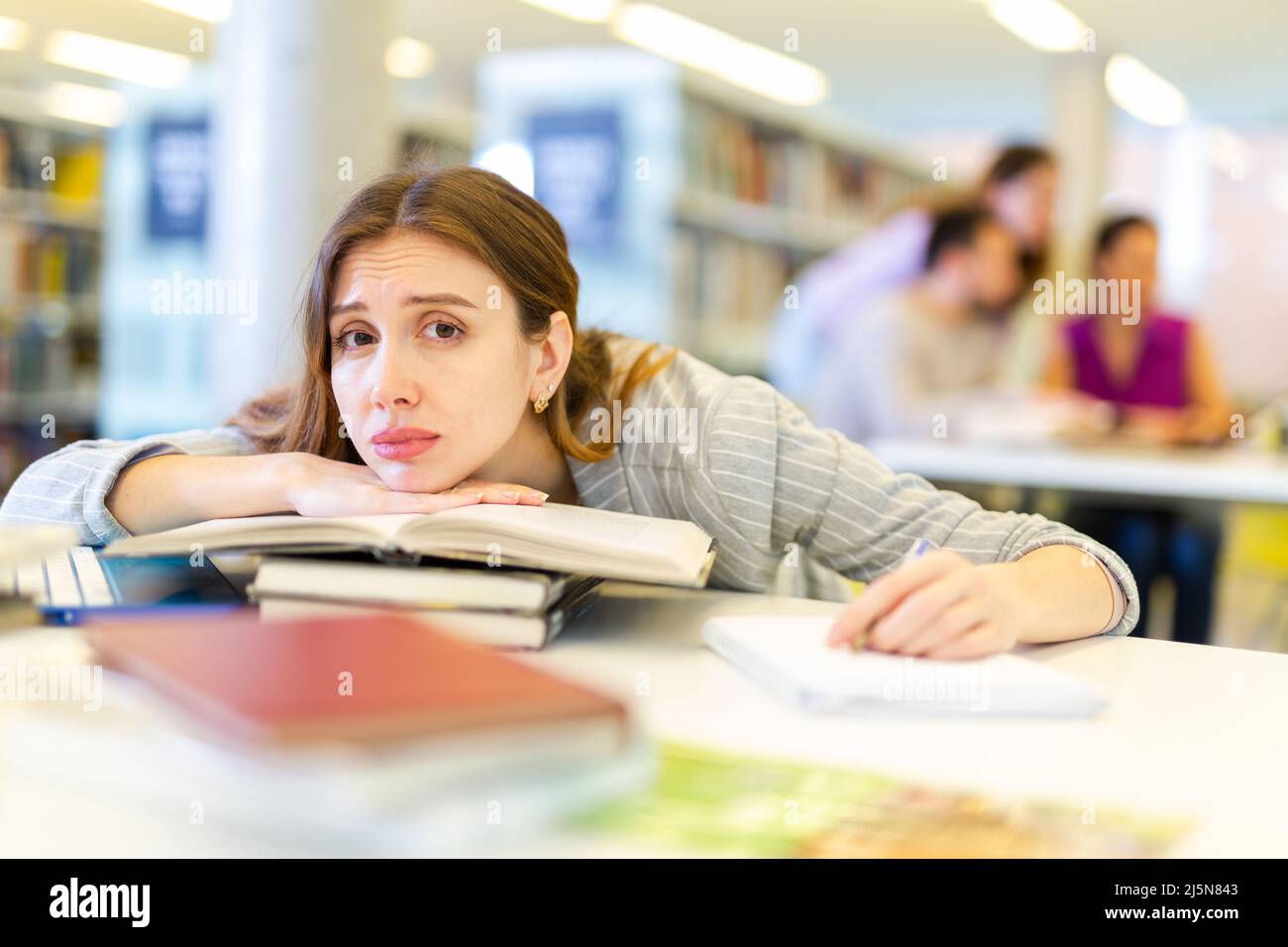 Tired young woman lying on stack of books in library Stock Photo - Alamy