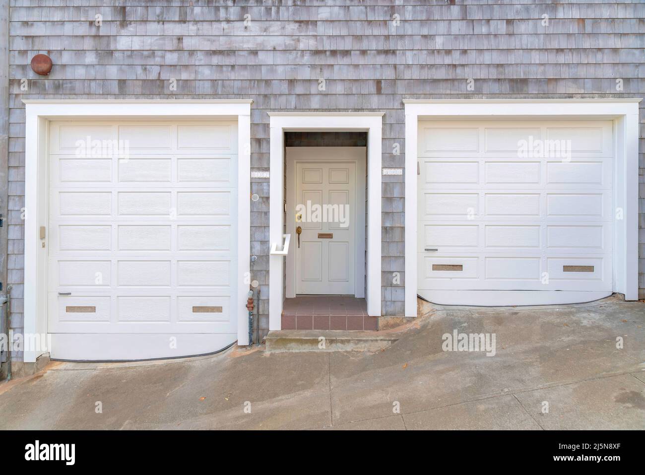 Facade of a house on a concrete slope with two white garage doors at ...