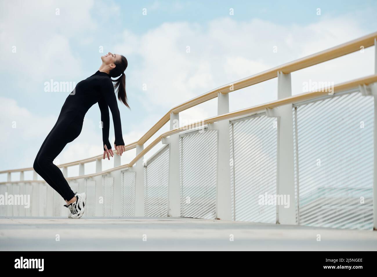 Happy female dancer in black jumpsuit doing toe stand on bridge Stock ...