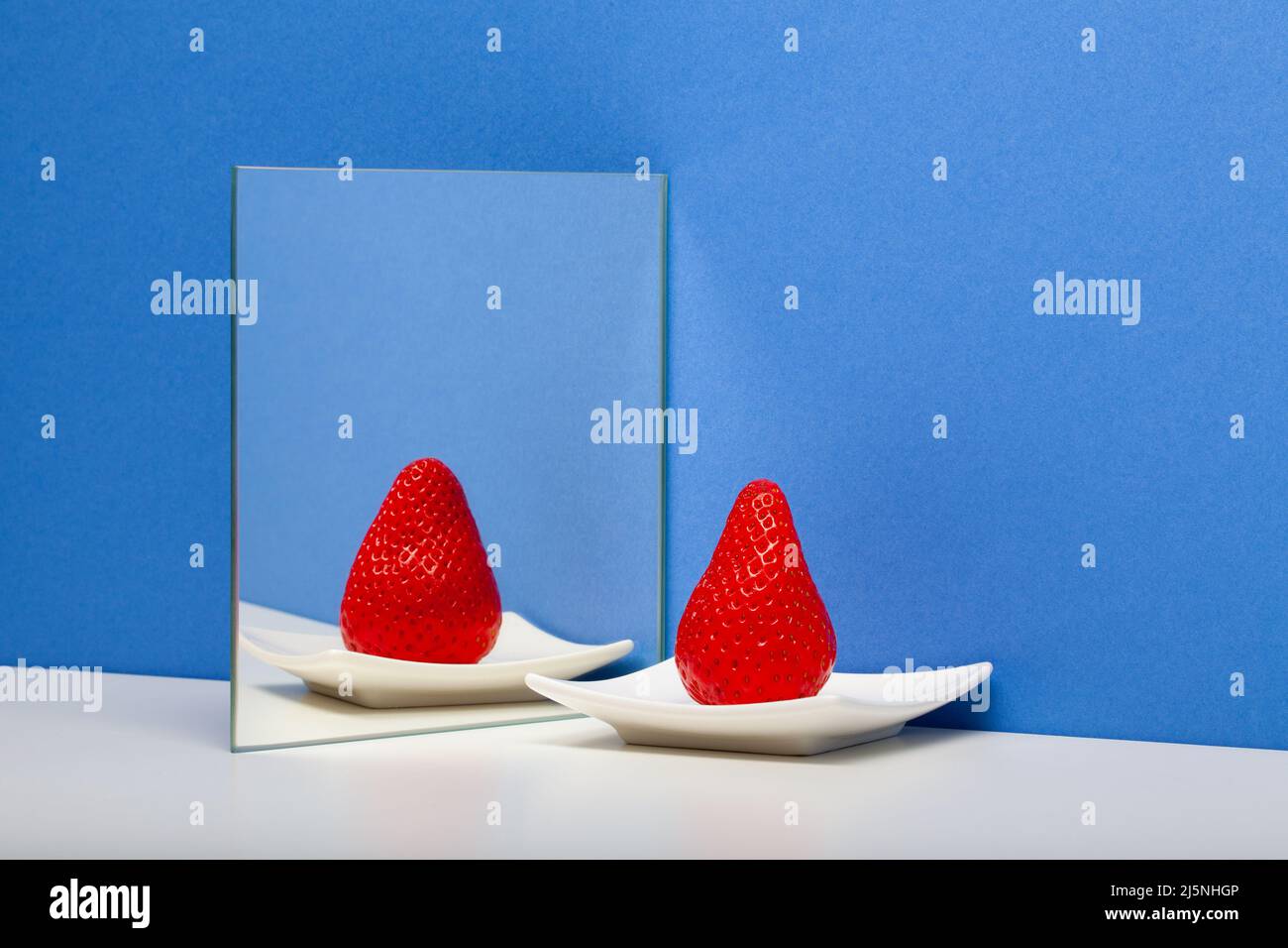A fresh and tasty strawberry reflected in the mirror on the blue ...
