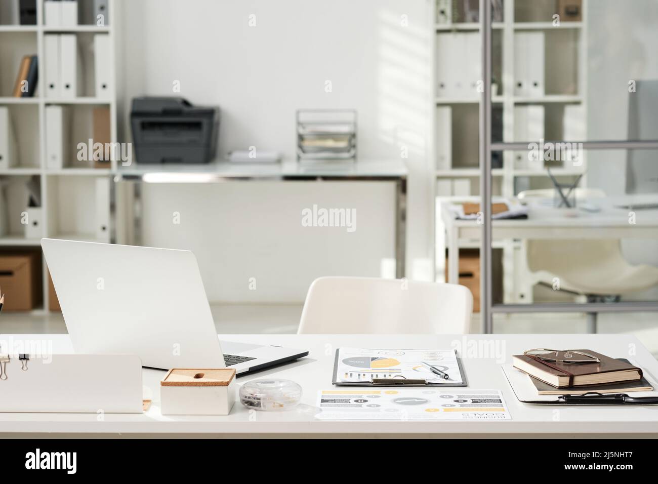 Office interior with white table with open laptop, financial documents ...