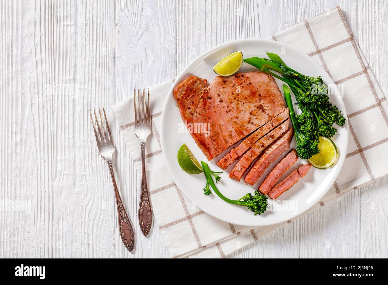 fried tuna steak with parboiled broccolini and lime on white plate on ...
